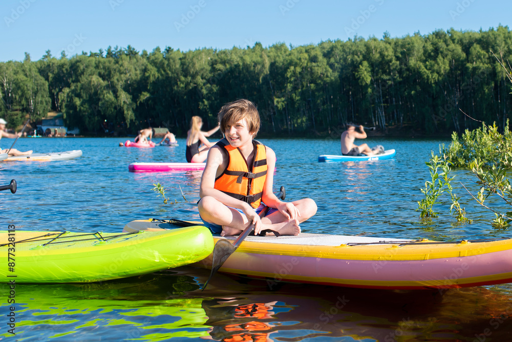An 11-year-old boy in a life jacket during a SUP swim on a lake among ...