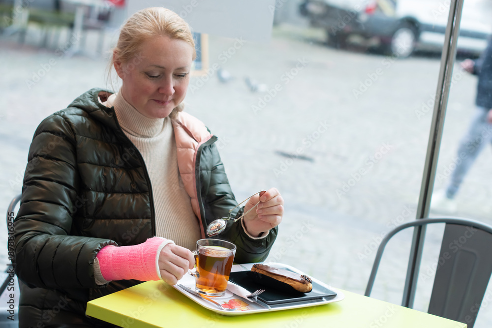 woman with a pink plaster cast on her right arm sits in a cafe and ...