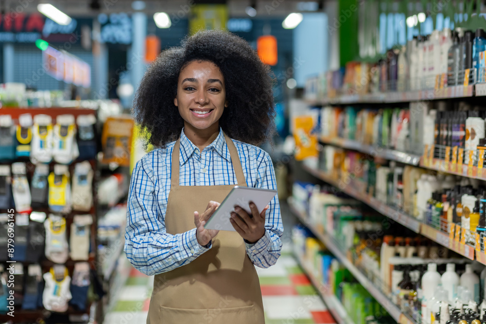 Female retail worker standing in store aisle holding tablet, smiling ...