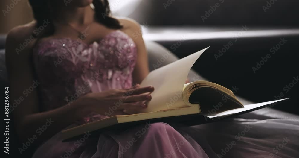 Elegant lady woman in a pink dress is reading a book sitting on sofa in ...