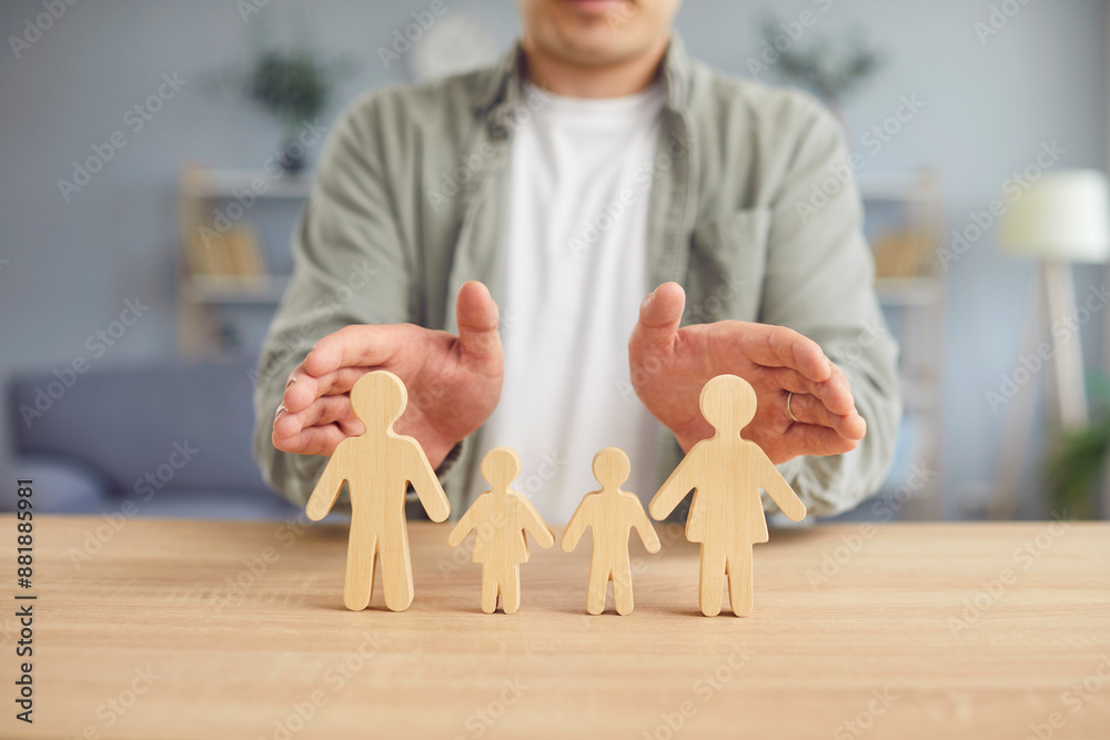 Cropped image of man guarding small wooden human figures, covering them ...