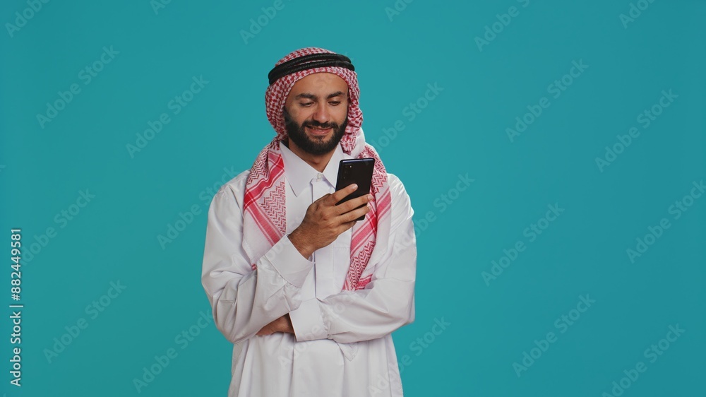Muslim man in traditional clothing using smartphone, engaged in online ...