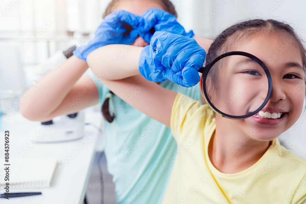 Joyful young girl hold magnifying glass up to her face, smiling widely ...