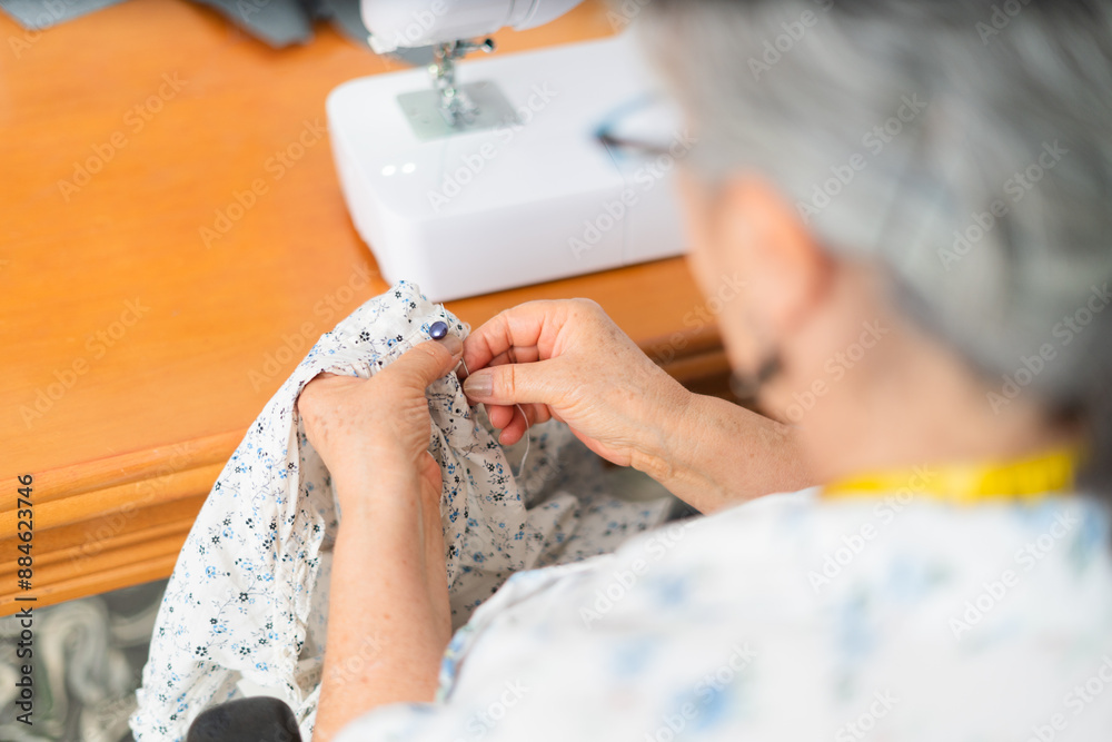 Unrecognizable senior woman sewing a button on a white floral shirt ...