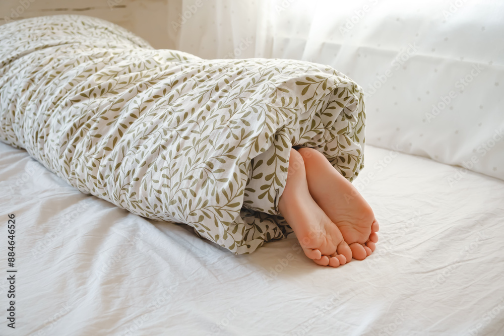 Rolled person. A child wrapped in a blanket with sticking out feet lies ...