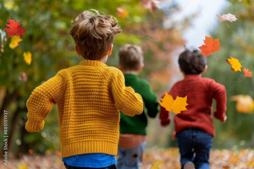 three young boys running through autumn leaves in a park - back view ...