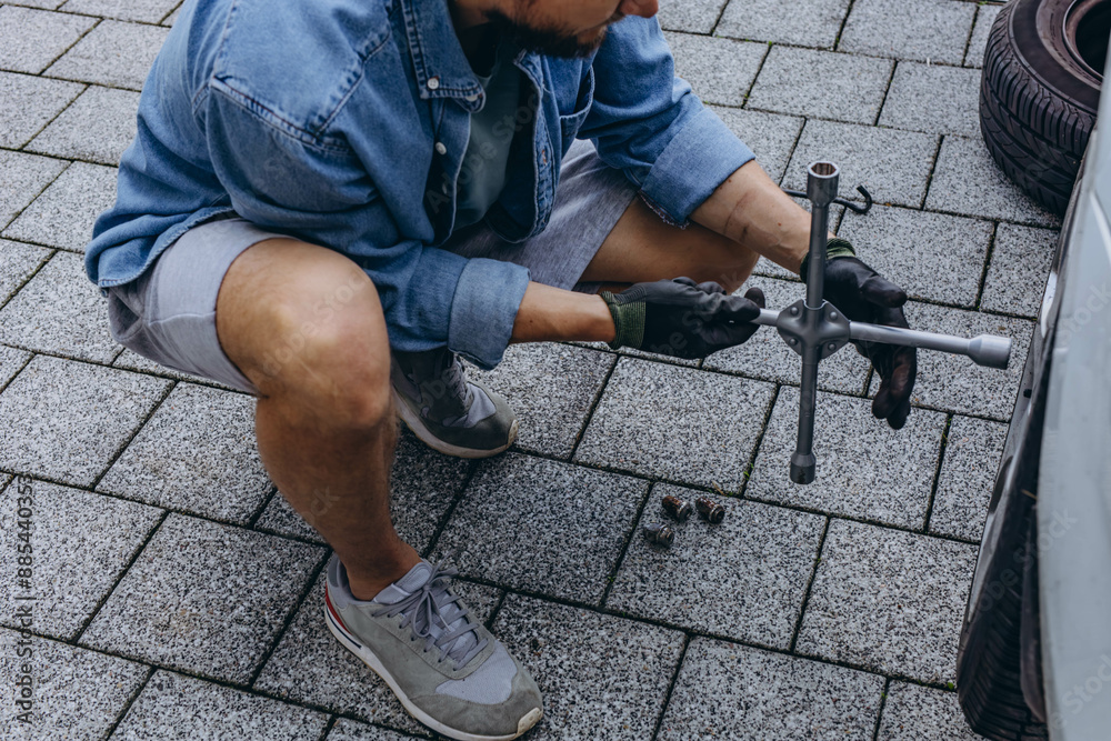 Young man in unscrewing lug nuts on car wheel in process of new tire ...