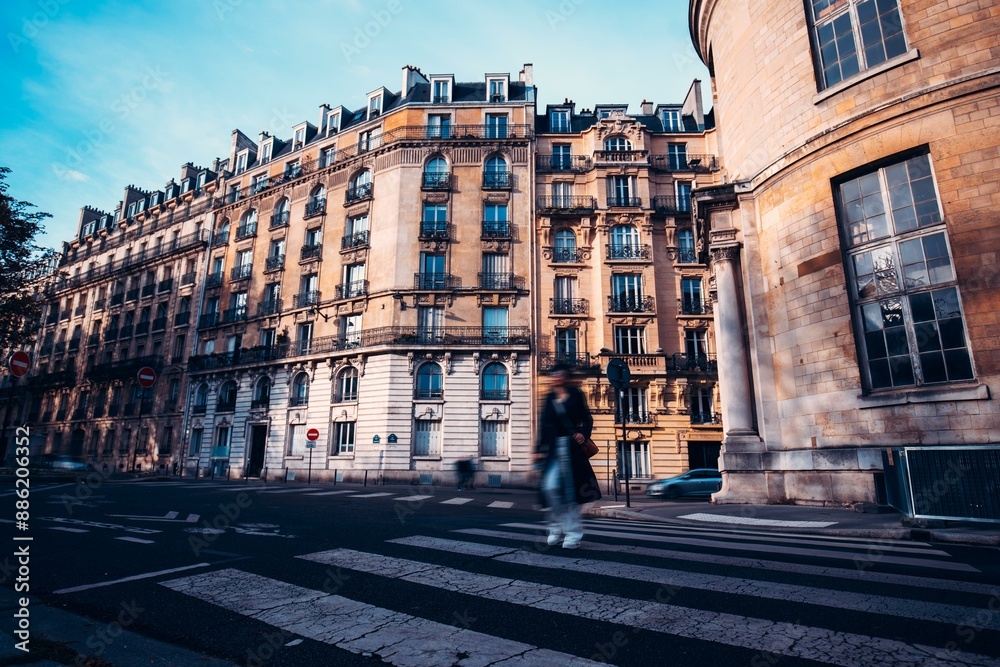 A pedestrian walks across a crosswalk in front of a classic Parisian ...
