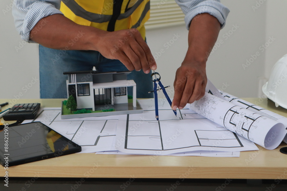 An engineer meticulously draws house plans on a workbench, surrounded ...