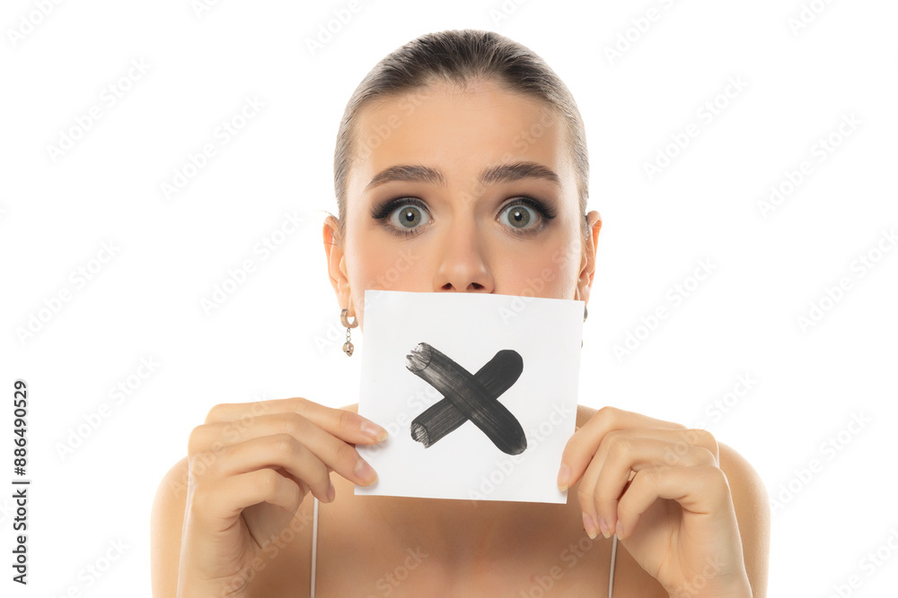 Beautiful young woman holding paper with cross symbol scared and amazed ...