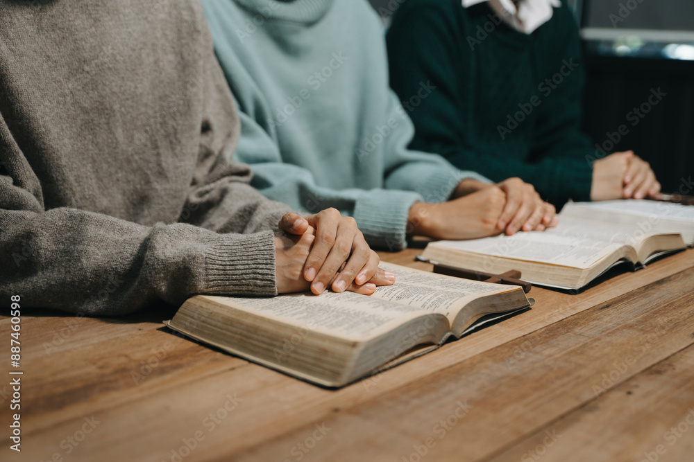 Group of Christians sit together and pray around a wooden table with ...