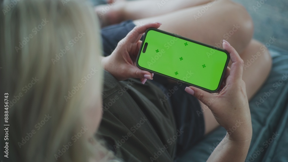 Back view of woman holding mobile phone with green screen and watching ...