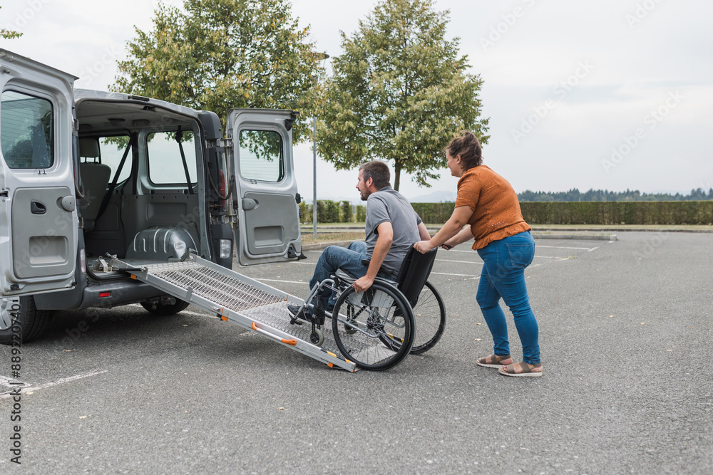 Female assistant helping a male person in wheelchair with transport ...