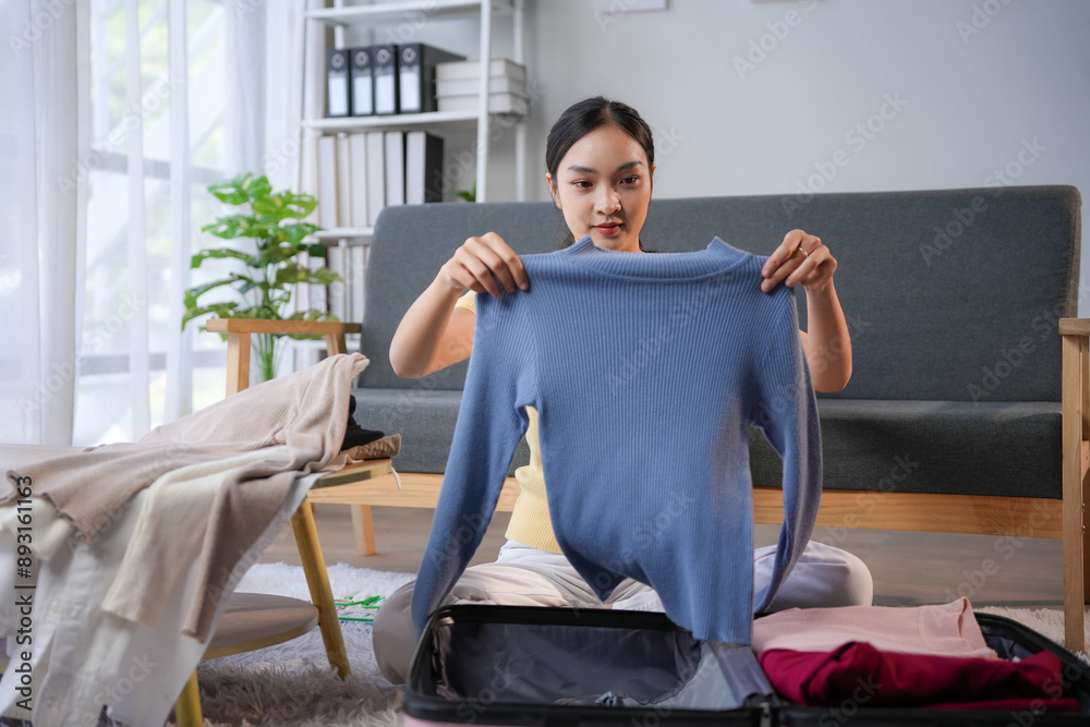 Young woman is packing for a trip, carefully folding and placing a blue ...