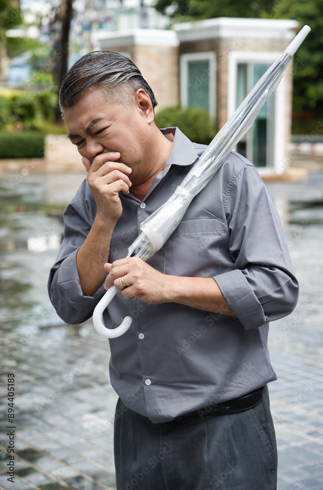 Asian middle-aged man carrying umbrella after raining, ill and sick ...