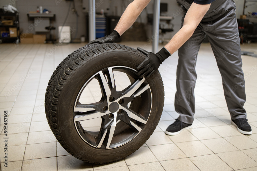 Mechanic handling car tire in automotive workshop. Person wearing ...