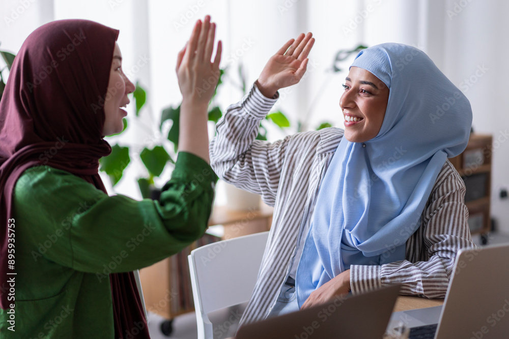Three women in hijabs high-five each other in a modern office They are ...