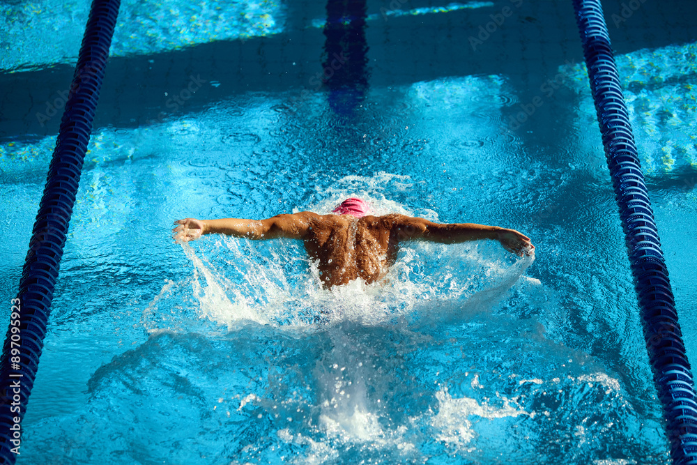 Overhead view swimmer in pink cap performs powerful butterfly stroke ...