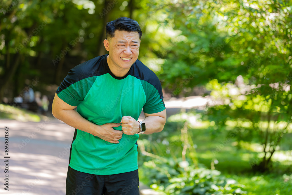 Middle-aged Asian runner feeling sudden strong abdominal stomach ache ...