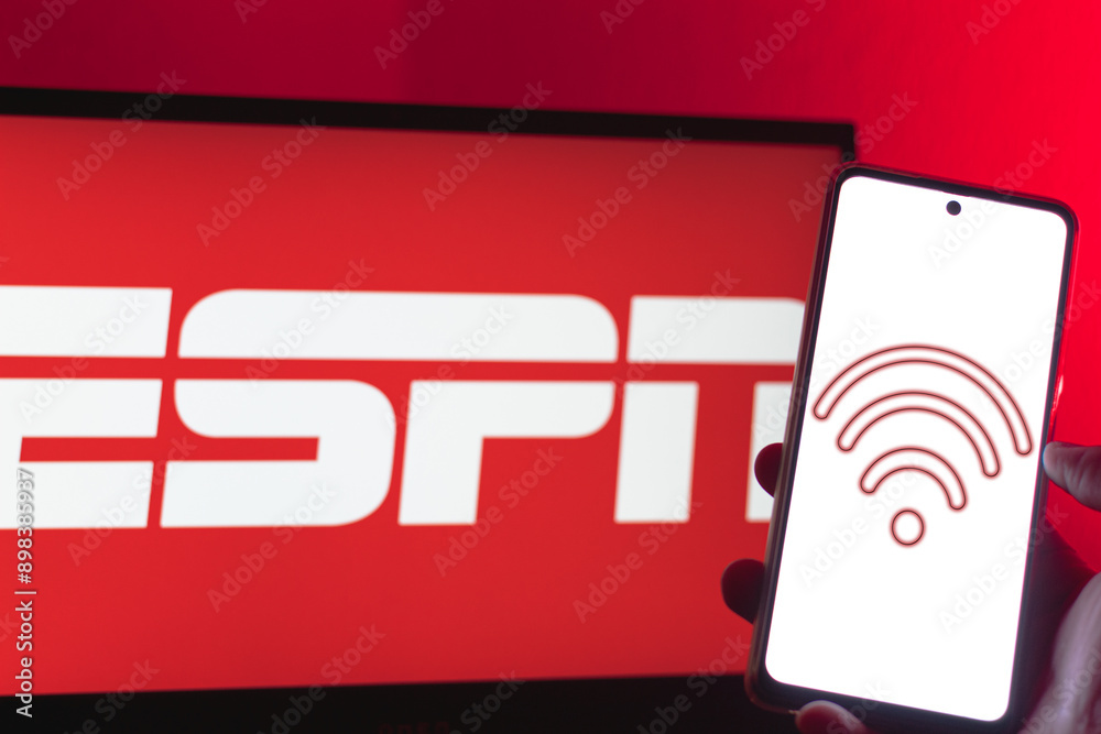 Cell phone with connectivity icon on the screen in front of a TV screen ...