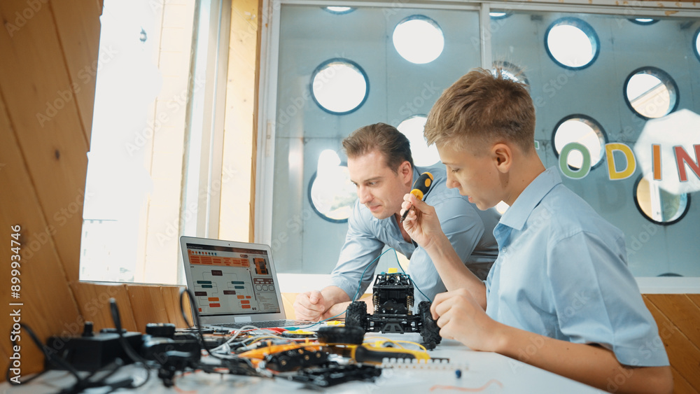 Caucasian teacher help student fixing car model and giving advise for programing system or ...