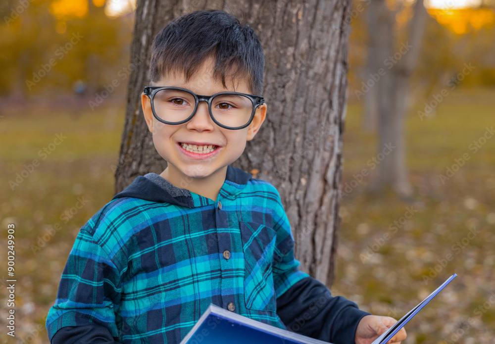 preschooler boy with glasses frame reading a book in park,leaning ...