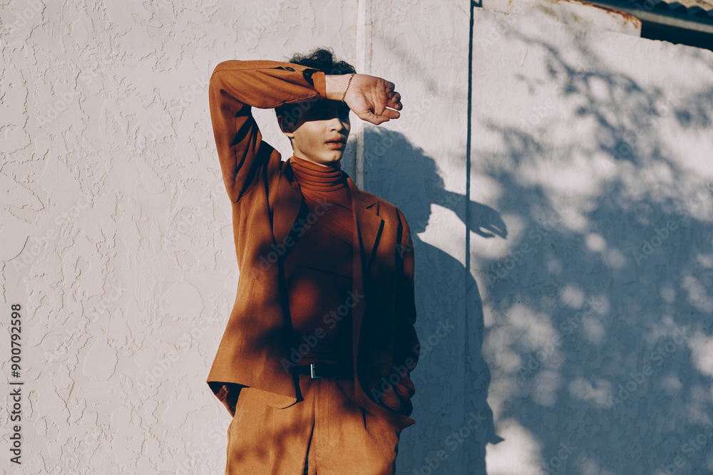 Stylish man posing with hand over face, wearing a brown outfit against ...