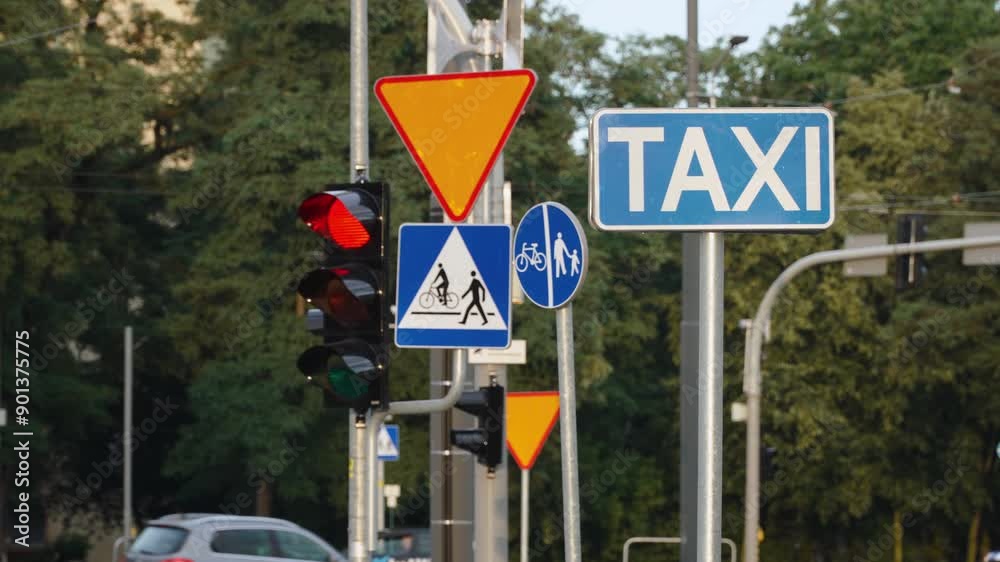 Many road signs at city intersection with red traffic light. Taxi stop ...