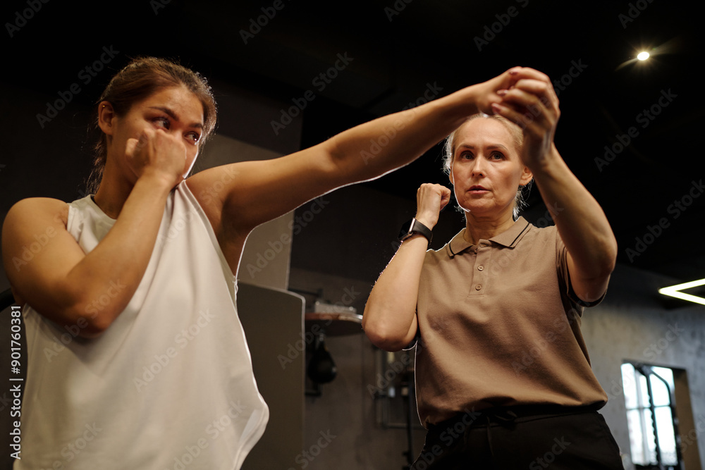 Experienced boxing trainer holding clenched fist of young female boxer ...