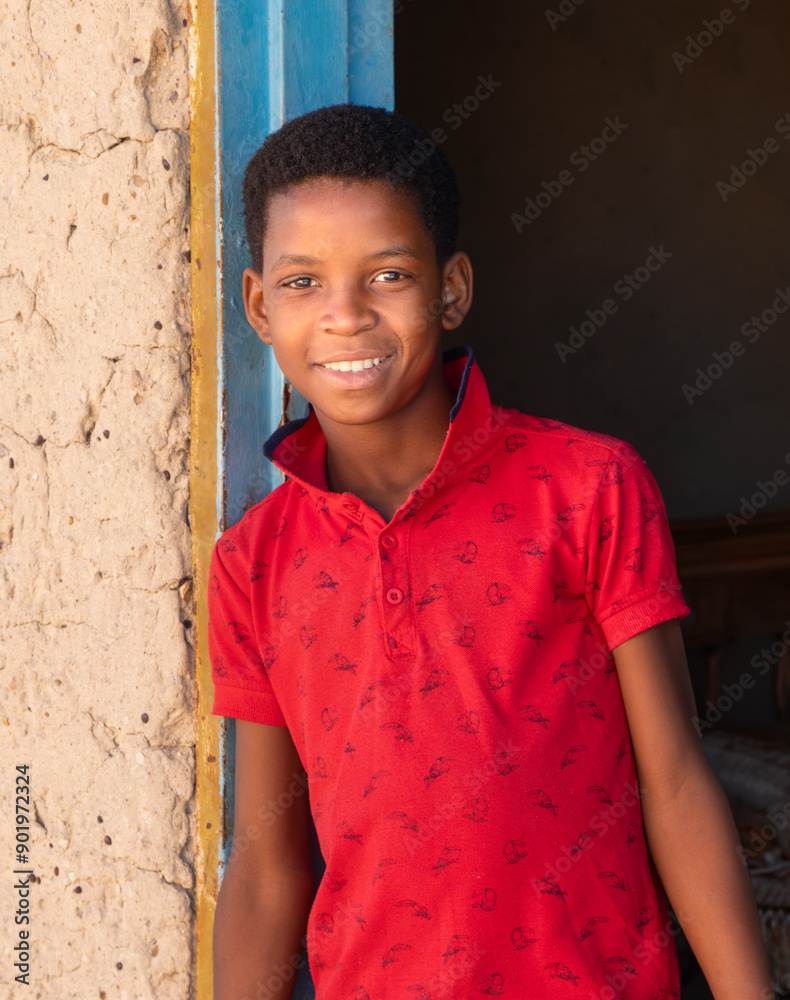 village portrait of a single african boy standing in front of the mud ...