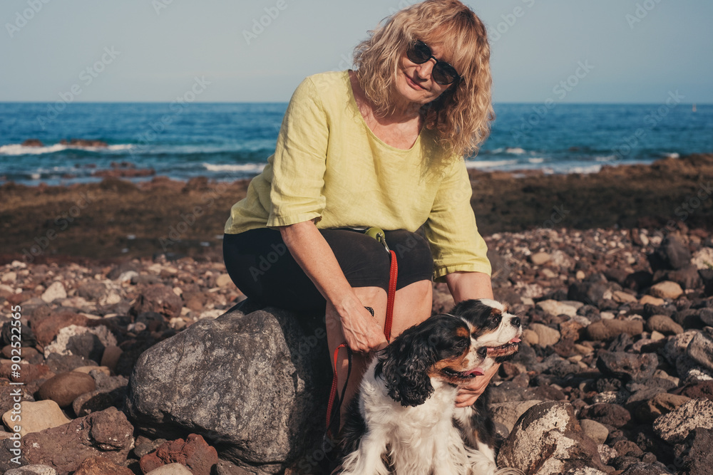 Handsome mature curly blonde woman sitting at the rock beach exchange ...