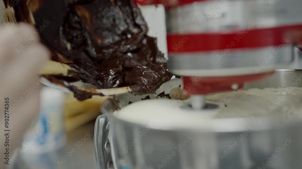Close-up shot of a baker pouring thick, dark chocolate batter into a ...