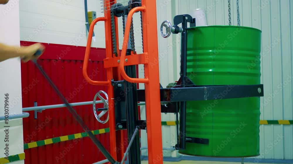 Factory worker in uniform lifts green barrel of chemicals using ...