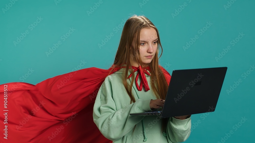 Young girl wearing superhero costume for Halloween working on laptop, isolated over studio ...