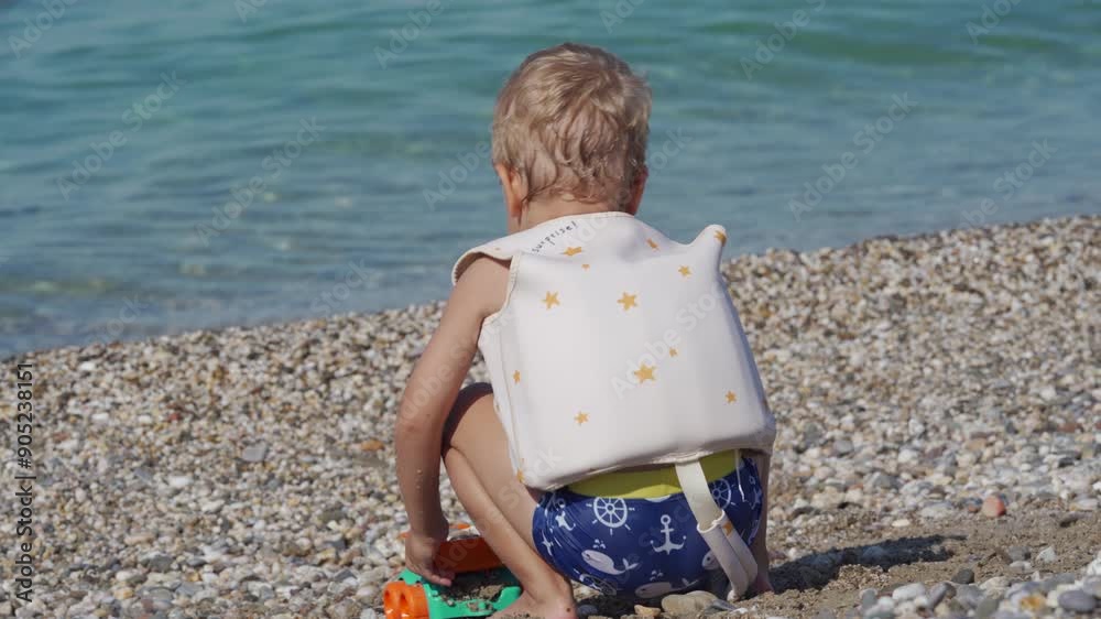 Happy little boy in swim vest life jacket playing on summer beach ...