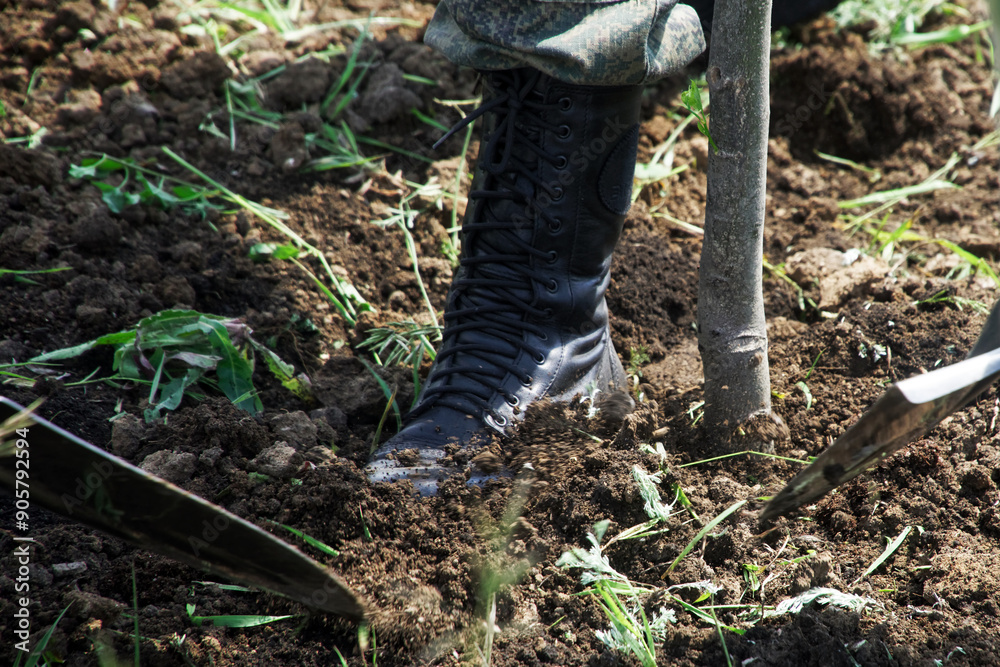 Man wearing high lace-up boots tamps down the ground next to a freshly ...
