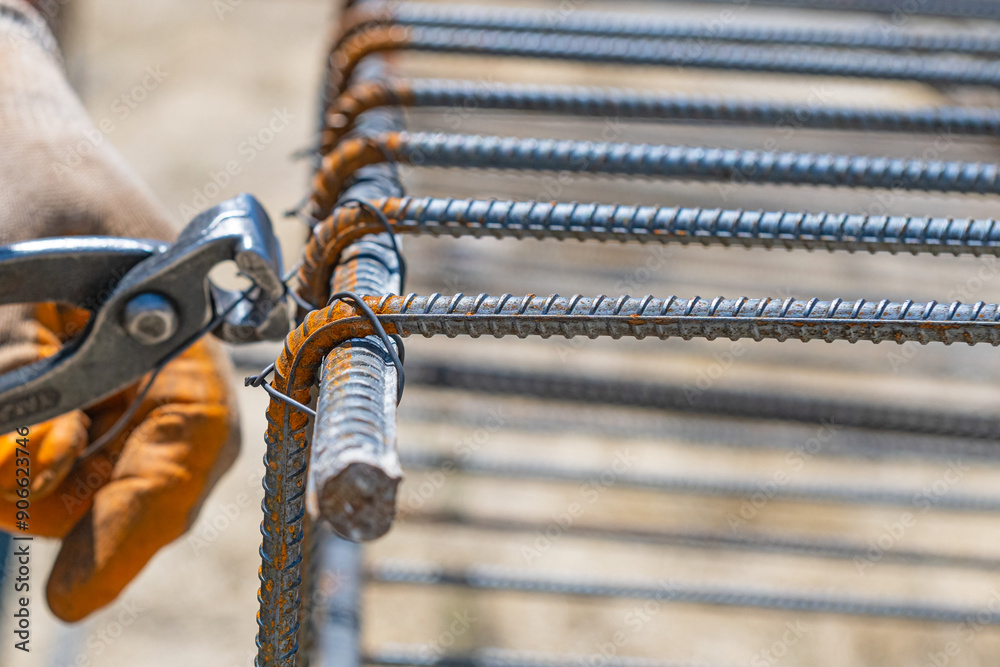 A worker uses steel tying wire to fasten steel rods to reinforcement ...