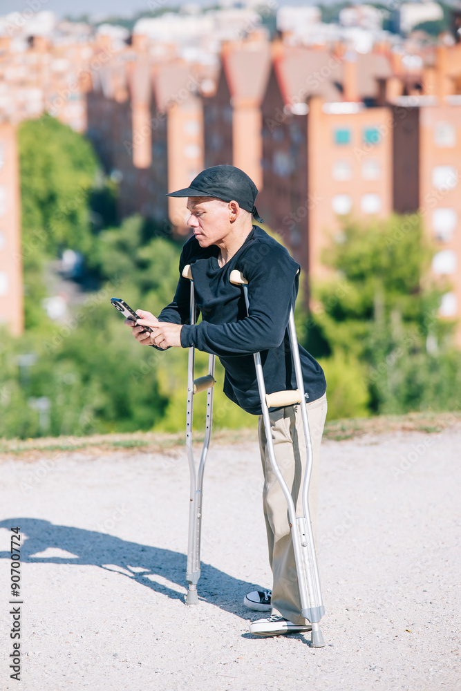 Person with a Motor Disability Using Crutches Looks at His Mobile Phone ...