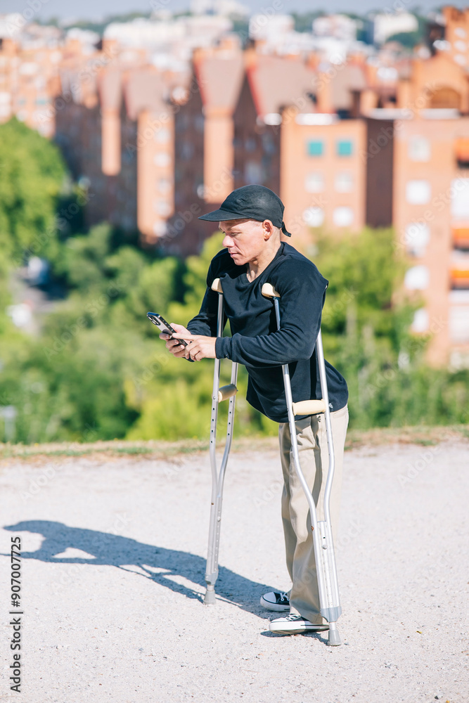 Person with a Motor Disability Using Crutches Looks at His Mobile Phone ...