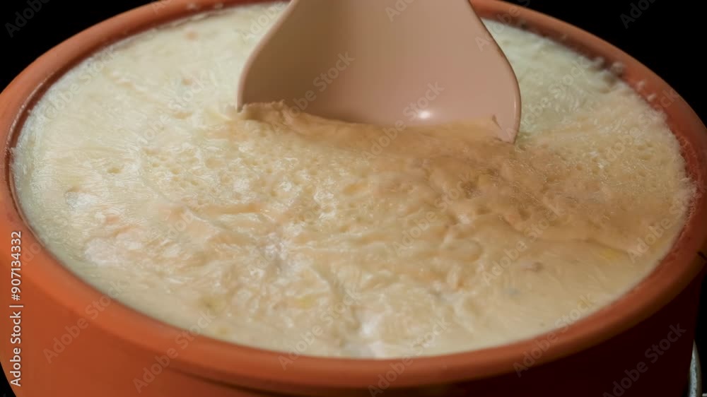 Close-up of yogurt being scooped from a traditional clay pot, featuring ...
