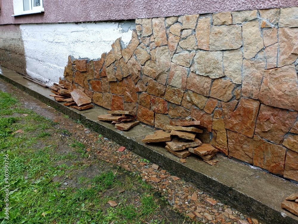 Sandstone stones are stacked near the wall of the house for its ...