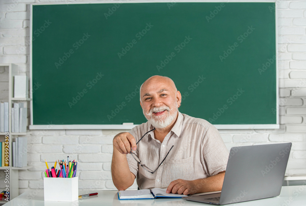 Portrait smiling man in glasses sit at desk. Old man teachers on green ...