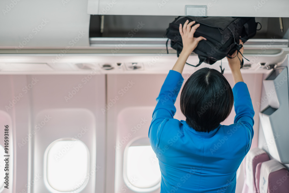 Flight attendant in blue uniform placing a black bag in the overhead ...