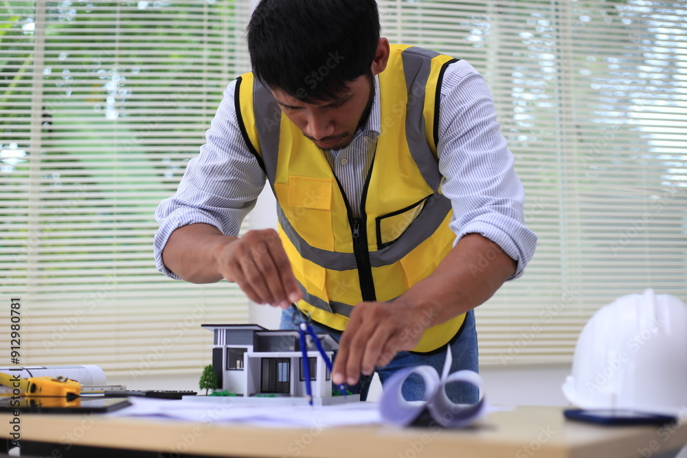 Asian architect and designer using blueprints and laptop to draw ...