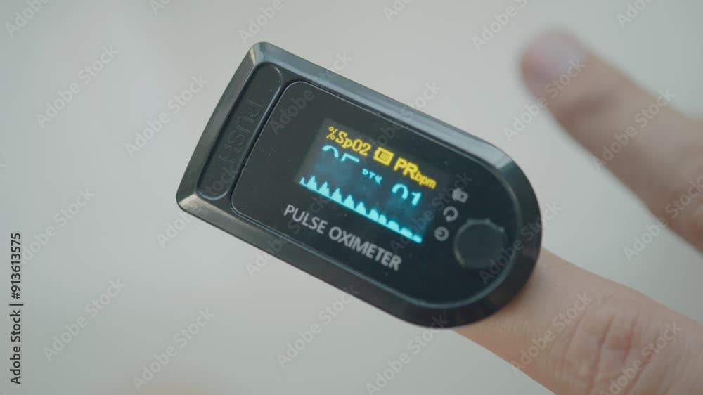 A finger is holding a pulse oximeter. The device is black and has a ...