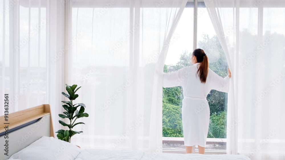 Woman wearing bathrobe opens curtains in bedroom and see around the ...