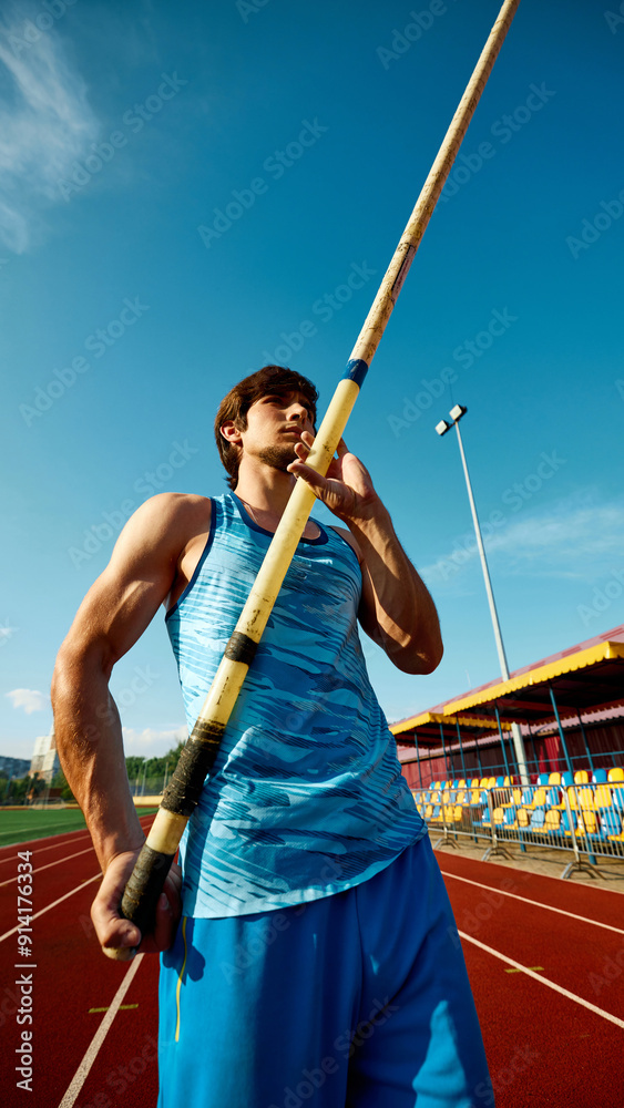 Pole jump athlete, focused young man in blue uniform standing with pole ...