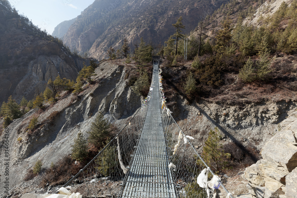 Narrow suspension bridge spans a deep valley with prayer flags ...
