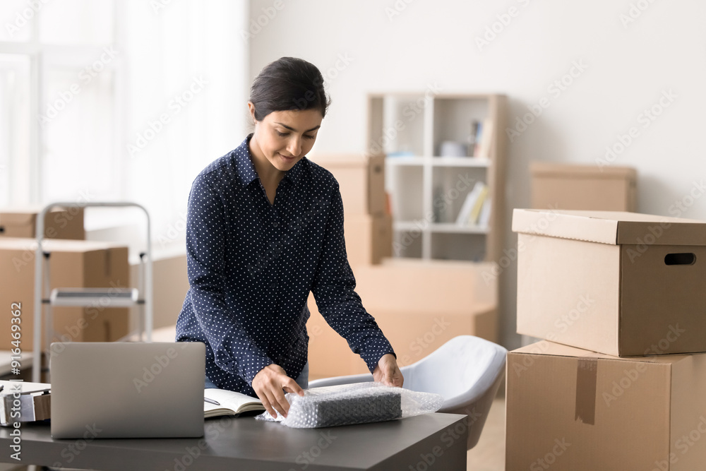 Serious young Indian woman, small business owner packing bought goods ...