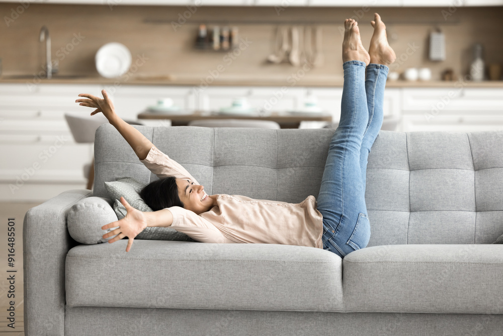 Happy woman enjoys relaxation lying on couch with legs raised and ...